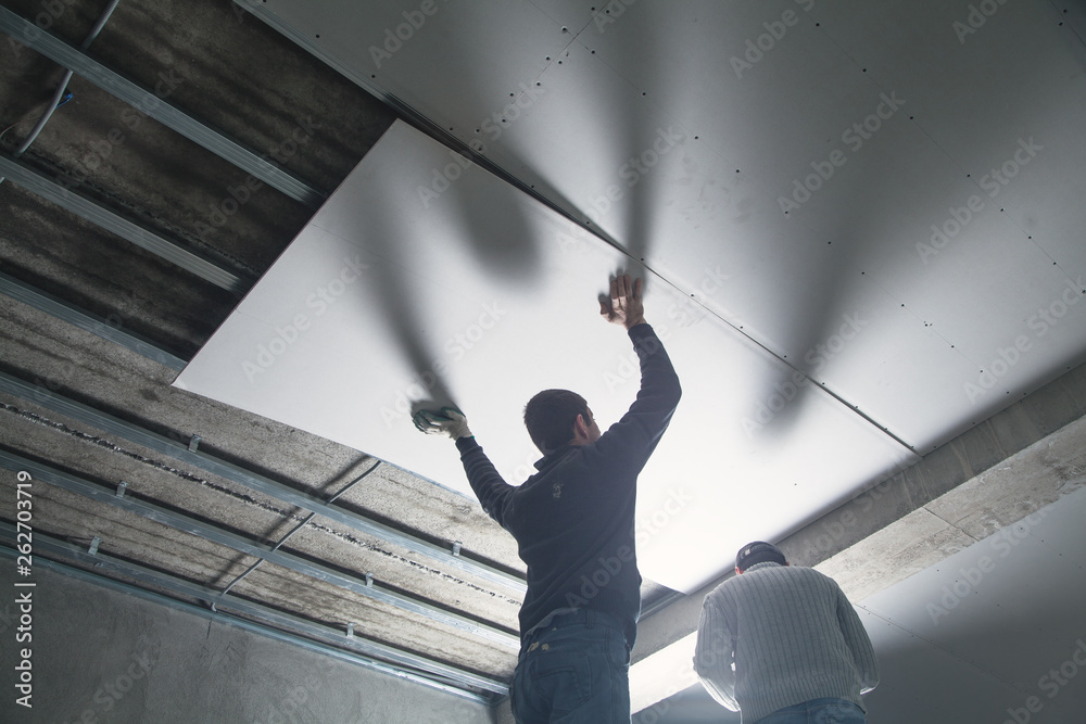 Workers fitting panel into frame of ceiling. Stock Photo | Adobe Stock