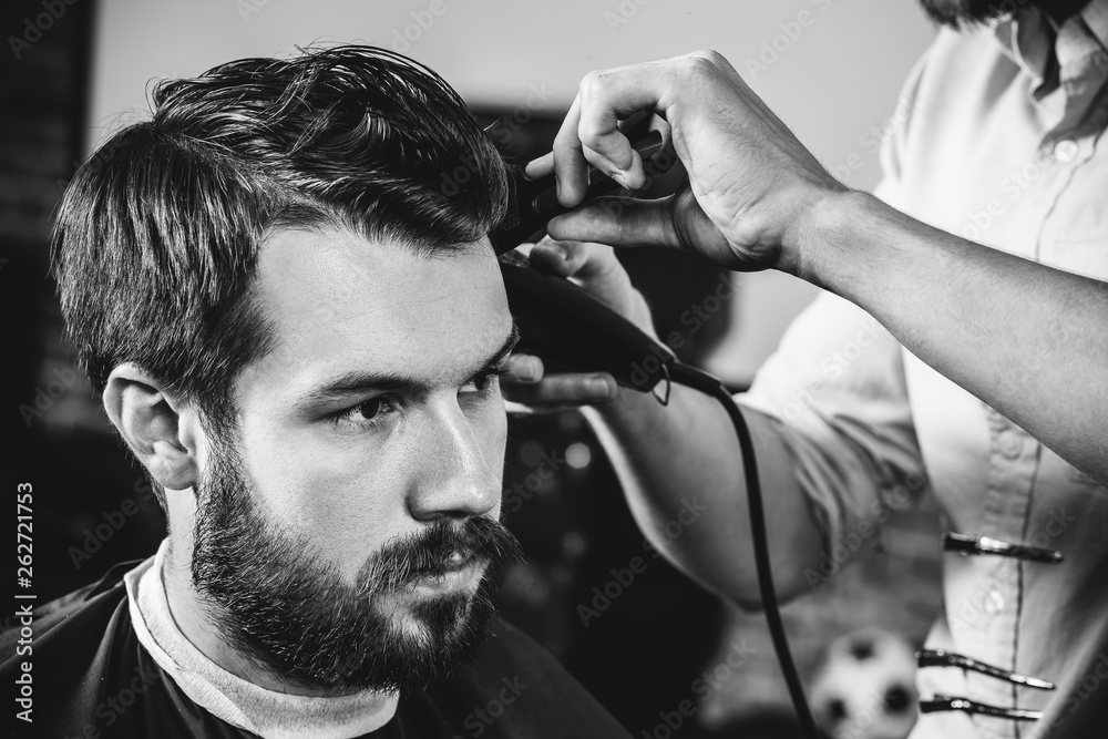 Young handsome barber making haircut for attractive bearded man at ...