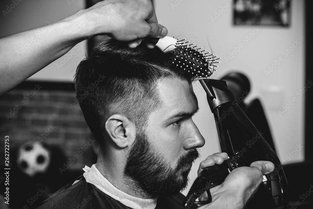 Young handsome barber making haircut for attractive bearded man at ...
