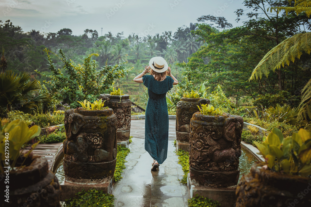 A young woman in a long dress and wearing a hat is standing with her ...