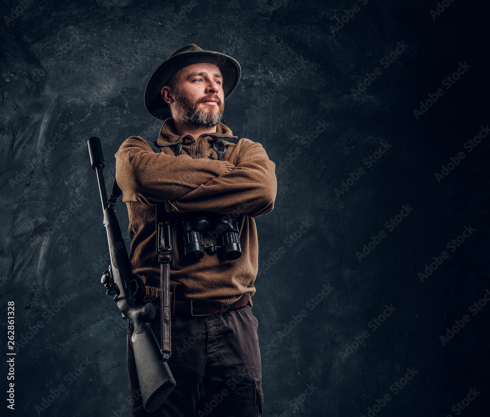 Portrait of a bearded hunter with rifle posing with his arms crossed ...