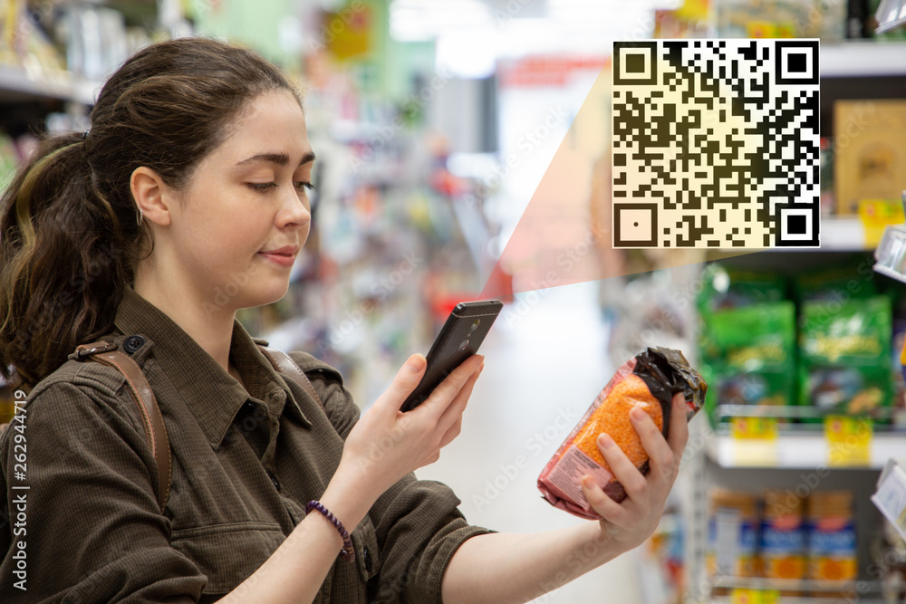 Young beautiful woman scans a QR code product in the supermarket. The ...