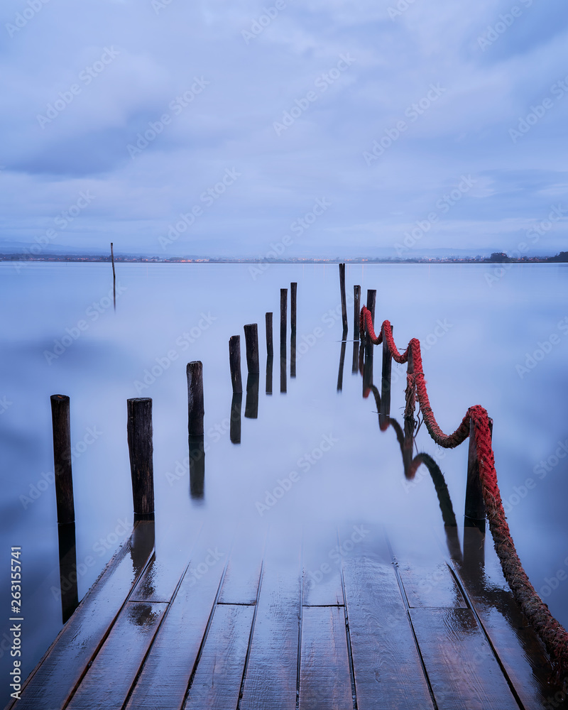 Palafitic pier submerged by the high tide at end of day, only the poles ...