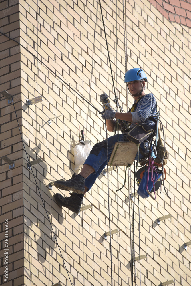 Industrial climber in helmet and uniform puttying wall on height. Risky ...