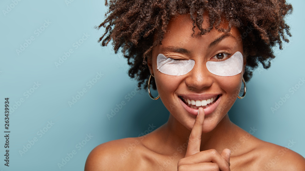 Happy female tells beauty secrets, blinks eye, has under eye patches ...