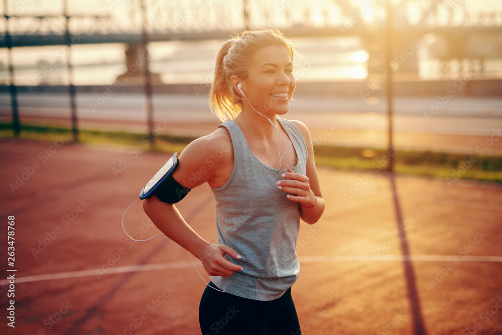 Charming female blonde runner in sportswear running on court with ...