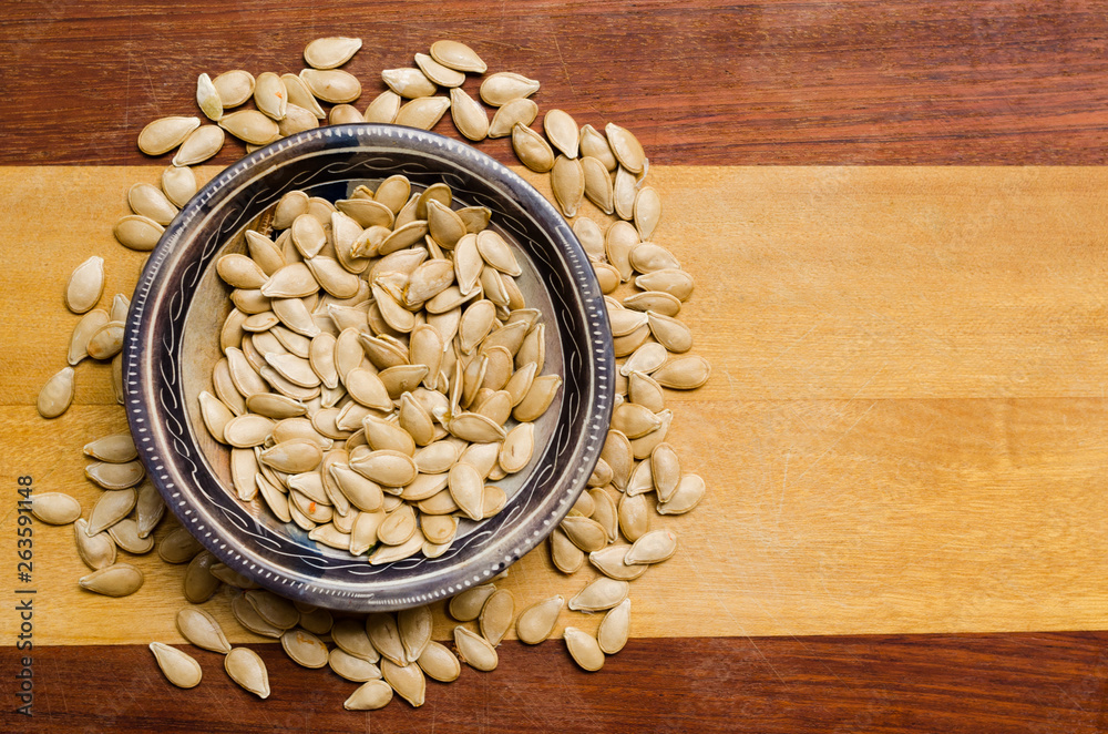 Pumpkin seeds inside a small bowl, some spread seeds below, on a two ...