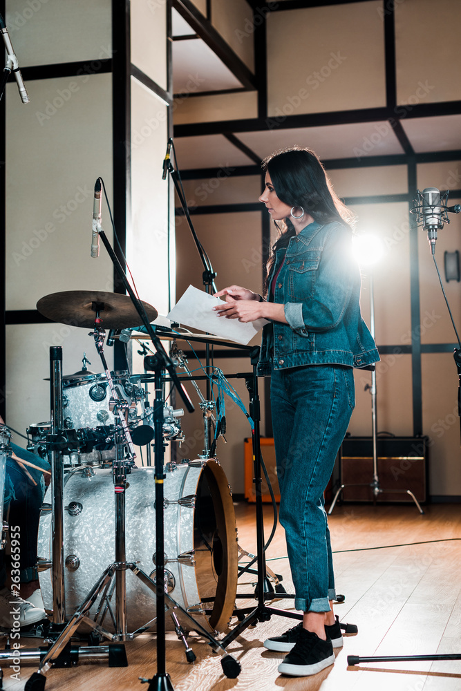 attractive singer standing near microphone and holding paper with text ...