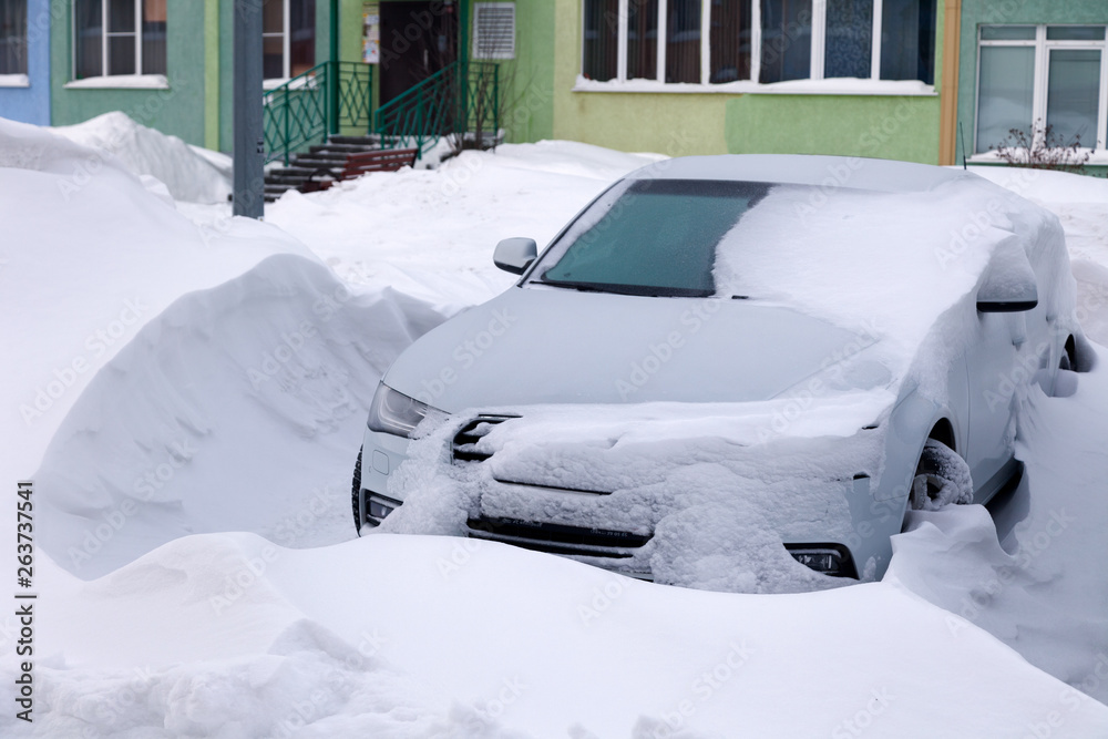 Сar covered with snow stands in parking lot of residential building in ...