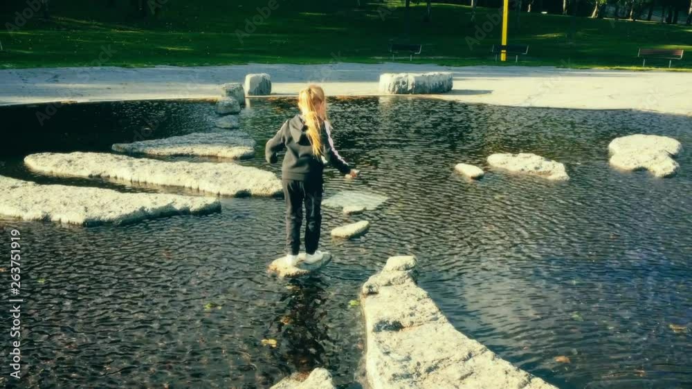 A little girl hops across rocks to cross a water feature designed for ...