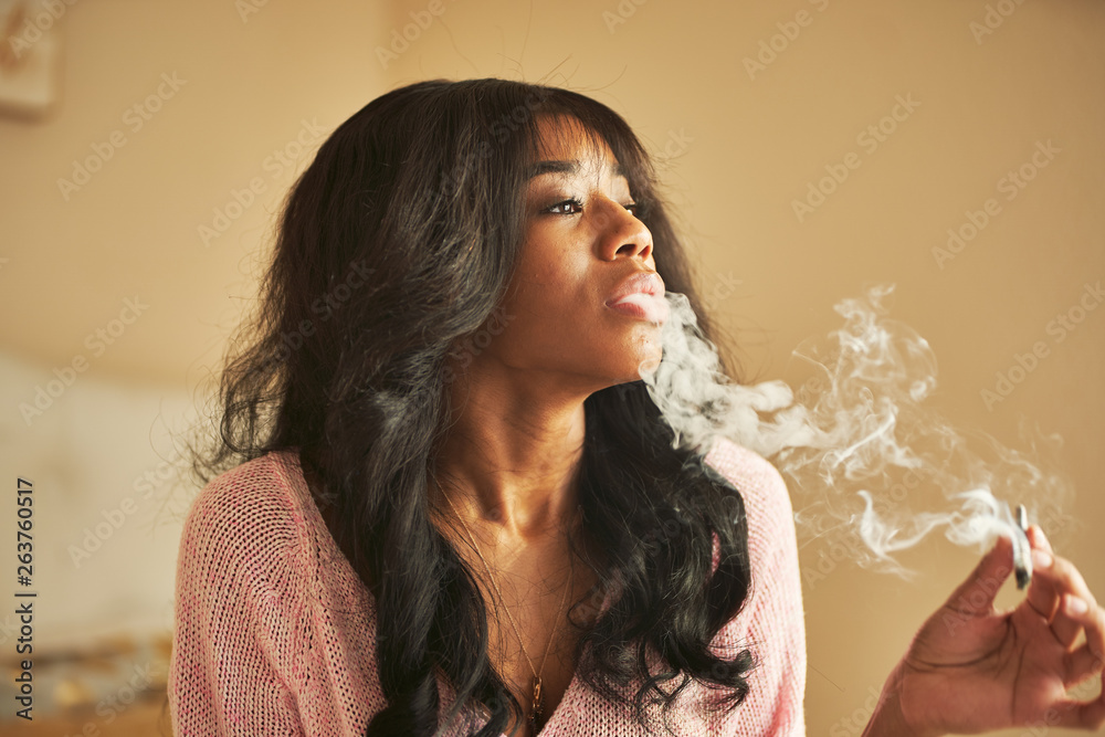 african american woman smoking marijuana joint while sitting on bed at ...