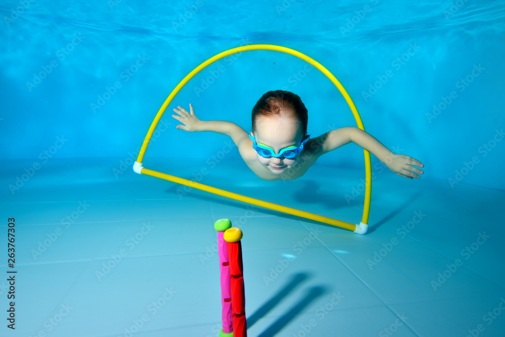 A little boy is engaged in scuba diving in the pool and dives for toys ...