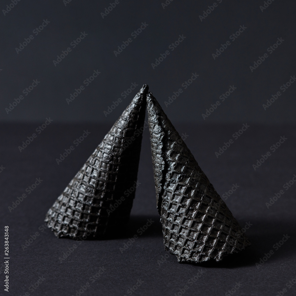Two waffle black cones for ice cream on a black paper background with ...