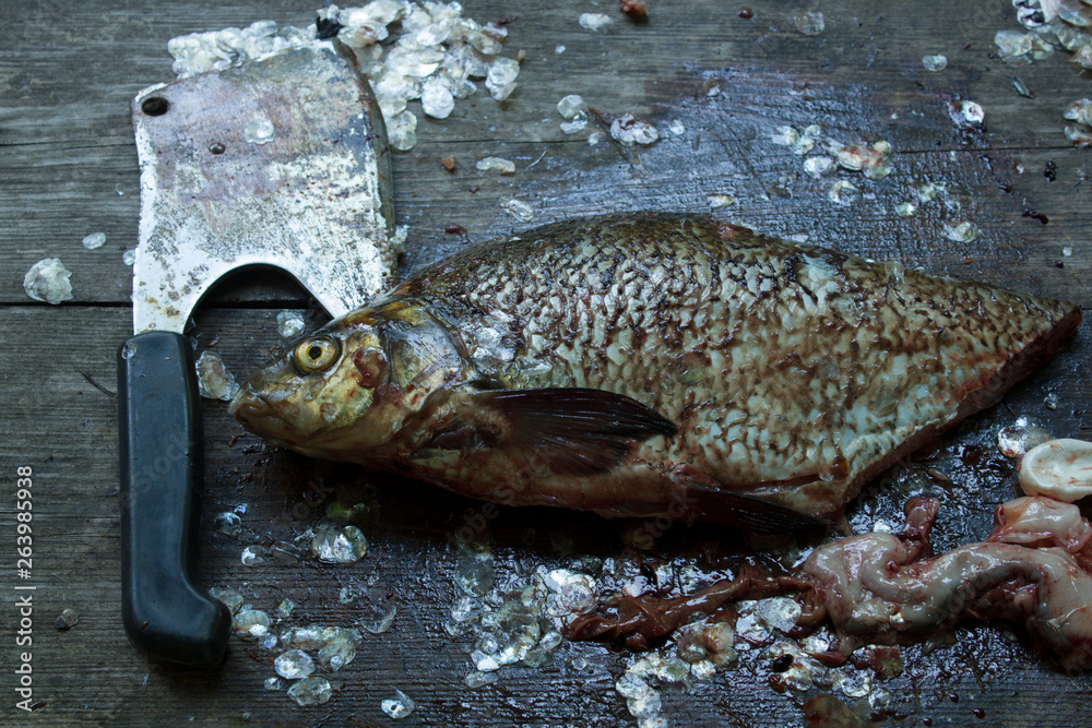 Hatchet and cleaned fish and its guts on a dirty weathered wooden ...