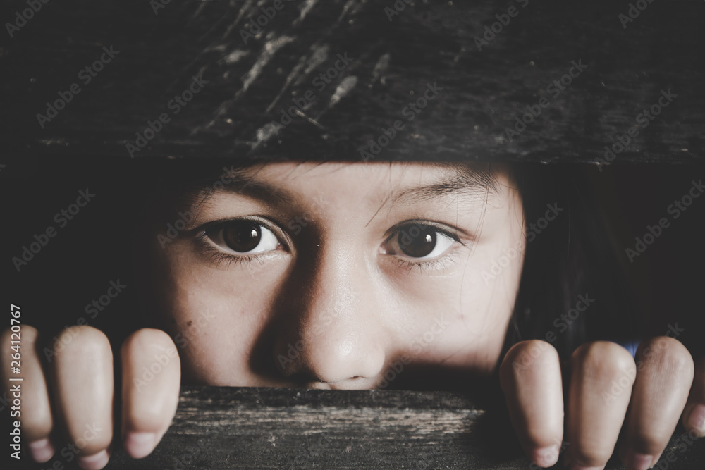 Bored little girl, Frightened child is spying through a wooden fence ...