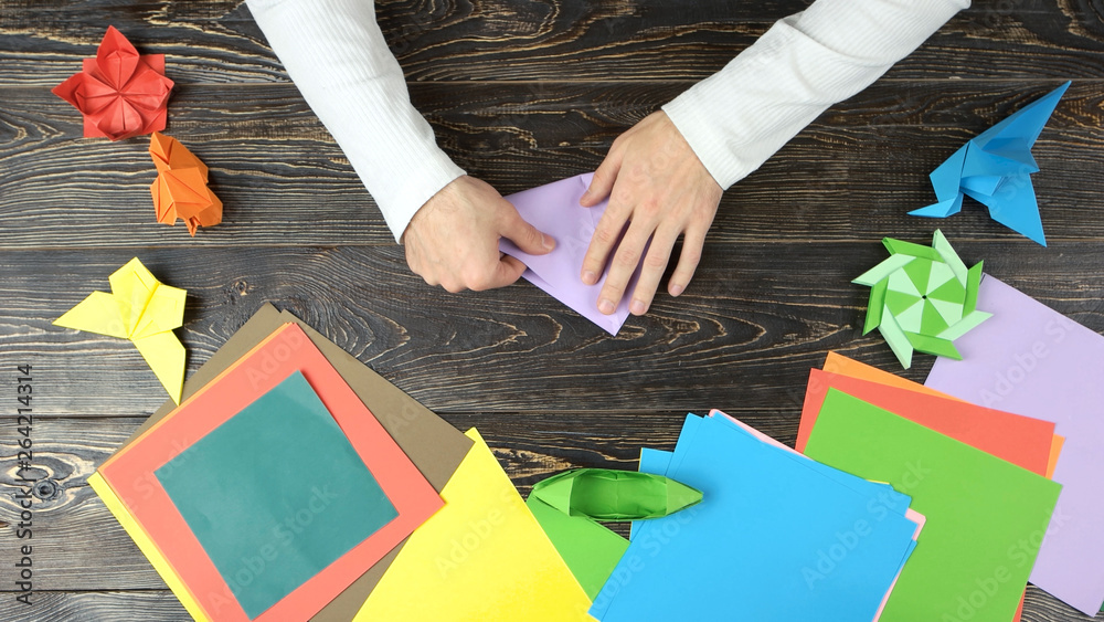 Man working at paper folding workshop. Hands making colorful lily from ...