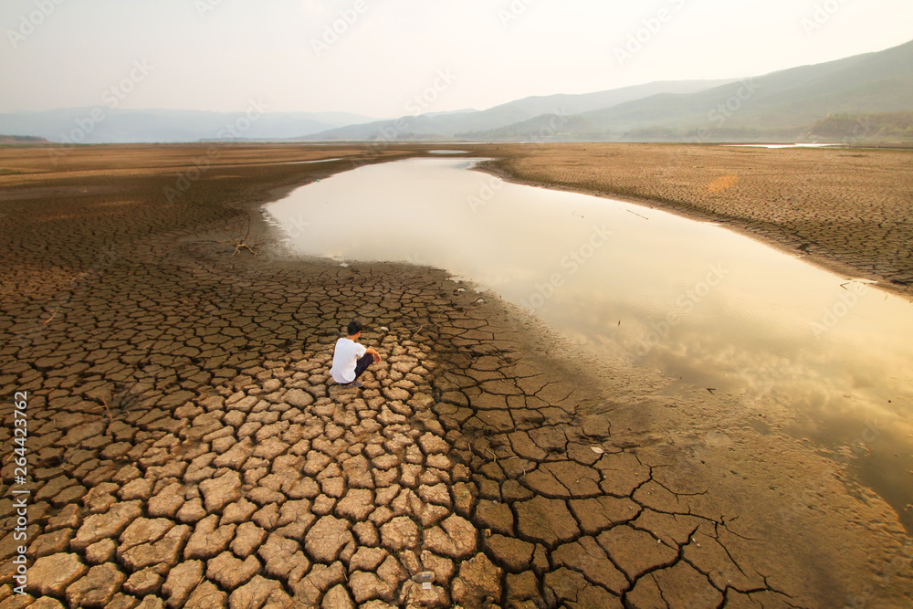 Sad man sit on cracked earth near drying lake in the summer. Climate ...