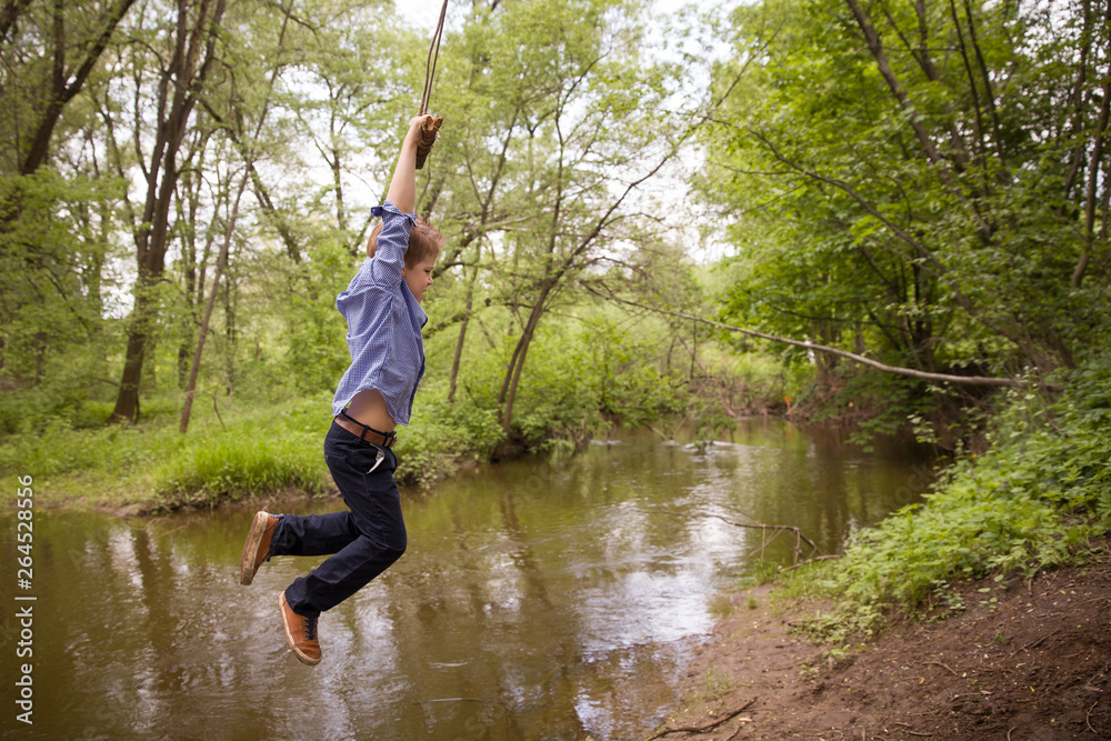 Fototapeta Cute boy rides a homemade bungee in the park. Bungee tied to ...