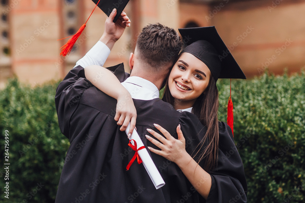 Graduates in mantles with diplomas in hands are standing near ...