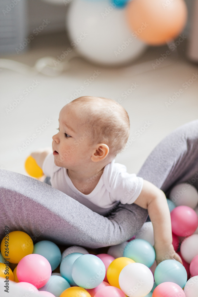 Cute one year old infant boy is playing with colourful balls in a dry ...