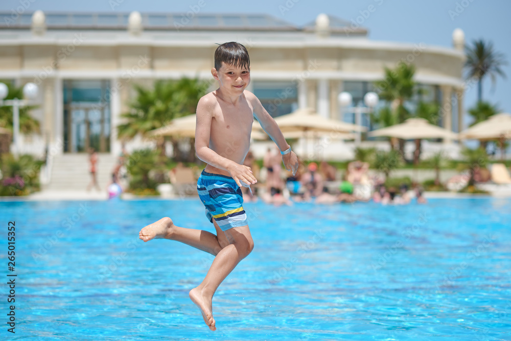 Smiling boy jumping into water in swimming pool. He is spinning in air ...