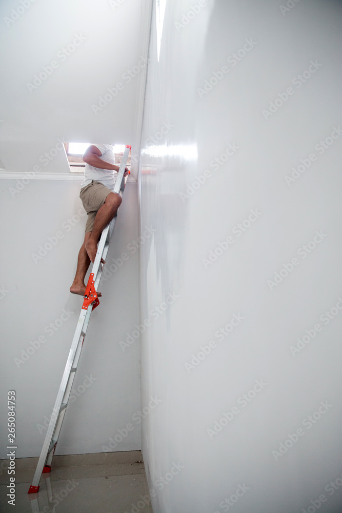 Asian young man using a ladder to repair the broken ceiling at home ...