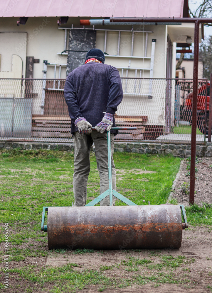 Adult man rolling heavy iron barrel for better condition garden after ...