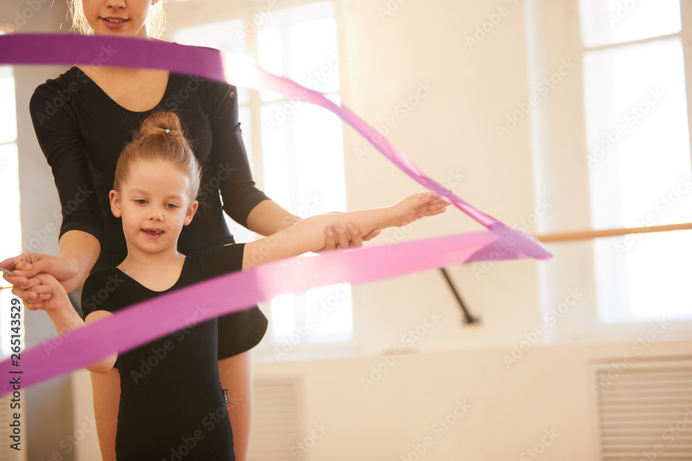 Little girl doing gymnastics moves with ribbon in studio lit by warm ...