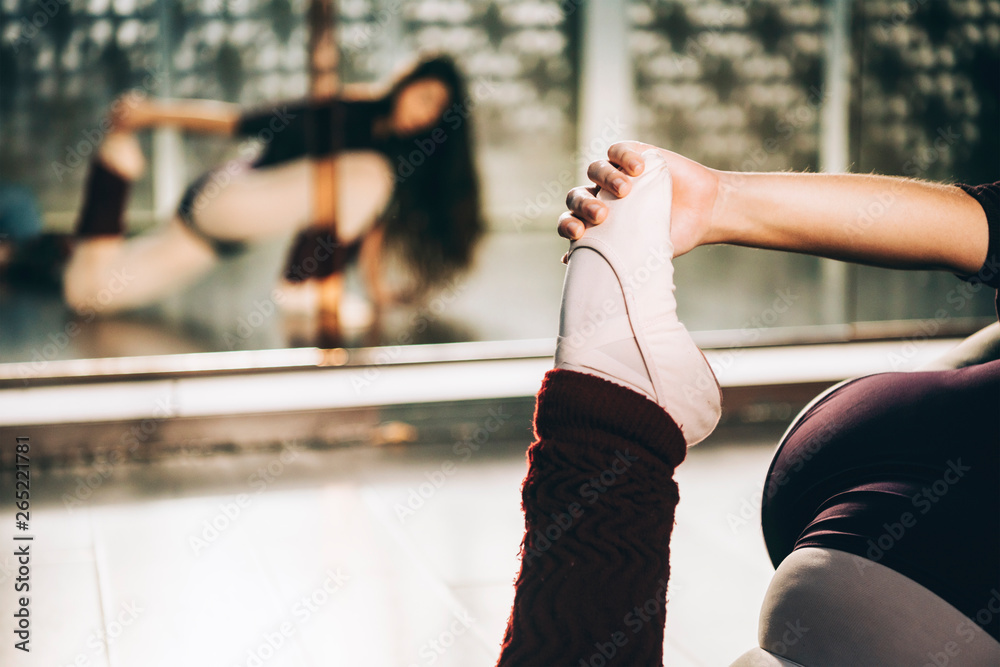 Crop shot of ballerina pulling leg to stretch muscles sitting on floor ...