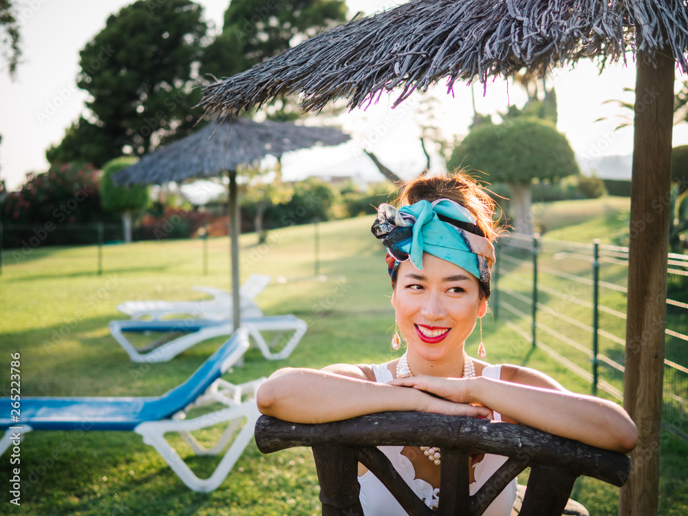 Young rich chinese woman sunbathing by a pool at a luxurious resort ...