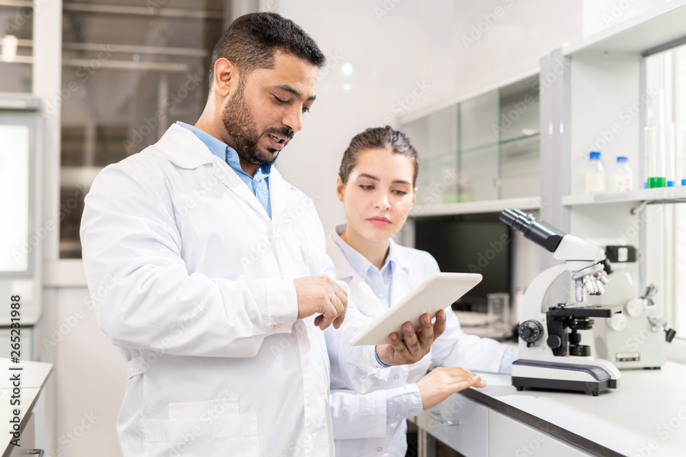 Confident experienced middle-eastern scientist in lab coat showing data ...