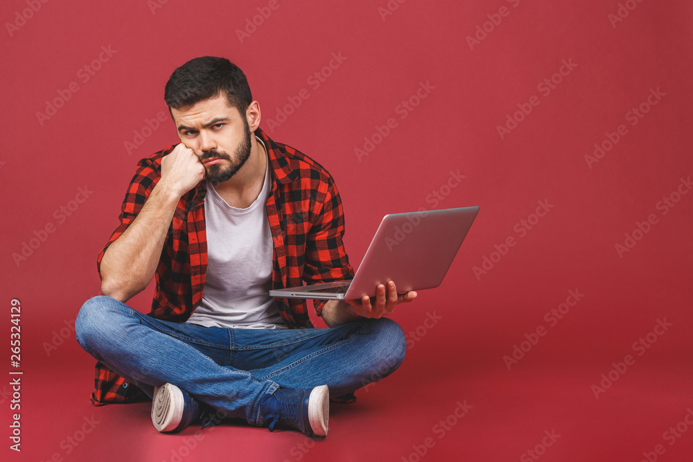 A young sad man sitting on the floor with a crossed legs putting his ...