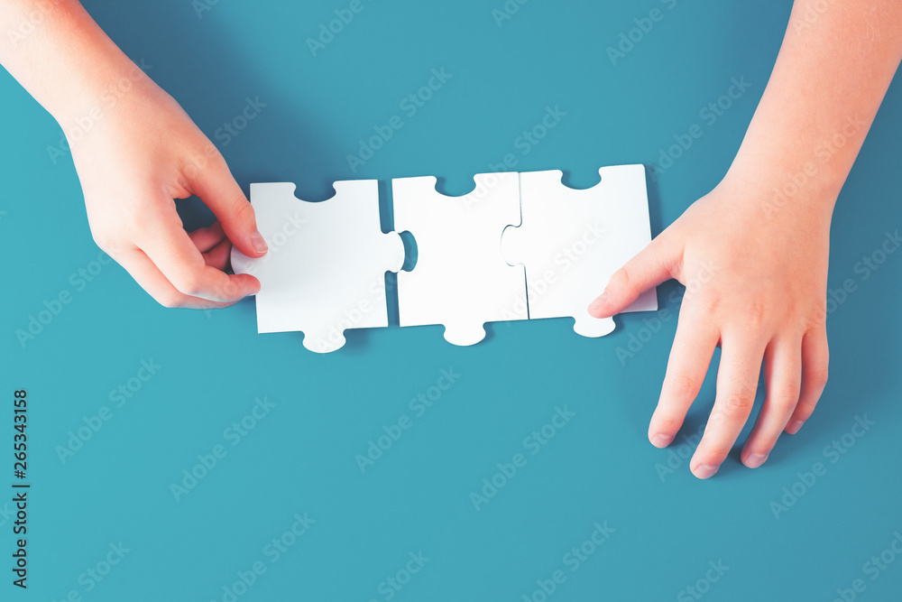 Jigsaw puzzle piece in one hand and another hand on the blue desk, top ...