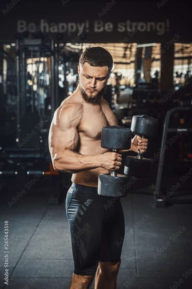 Good looking young man bodybuilder lifting dumbbells working on his ...
