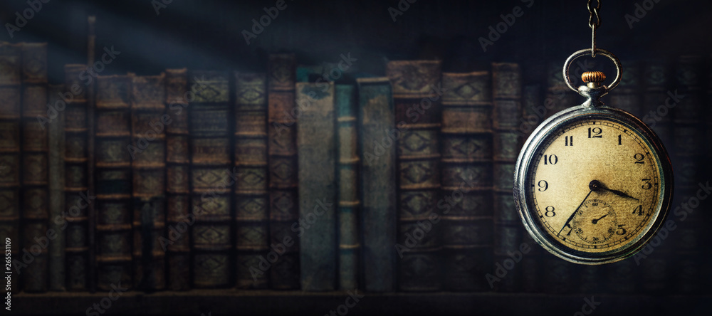 Vintage clock hanging on a chain on the background of old books and sun ...