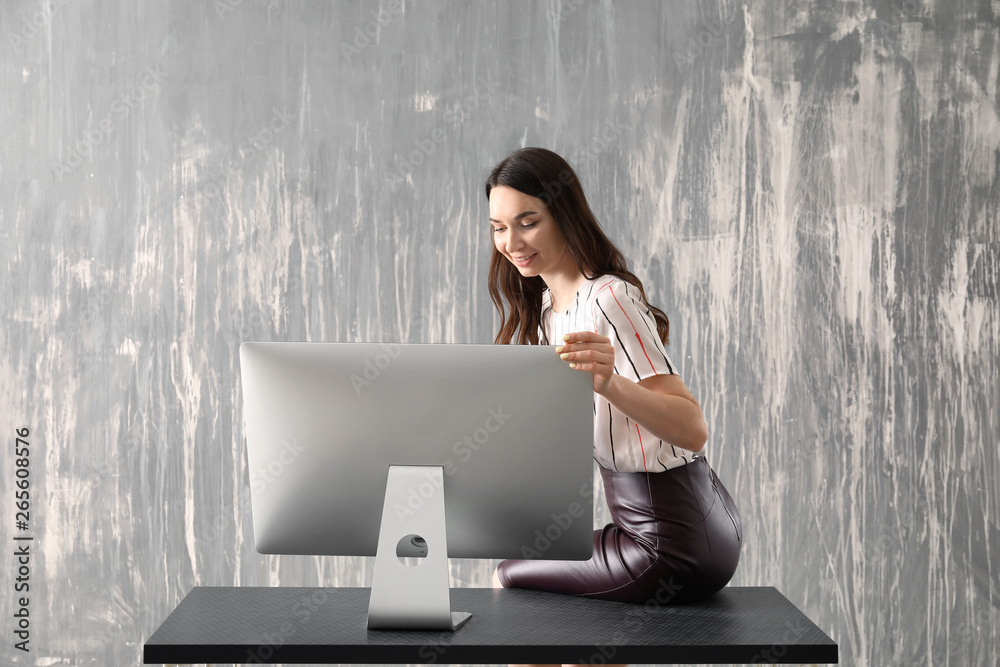 Beautiful young woman with computer sitting on table against grey ...