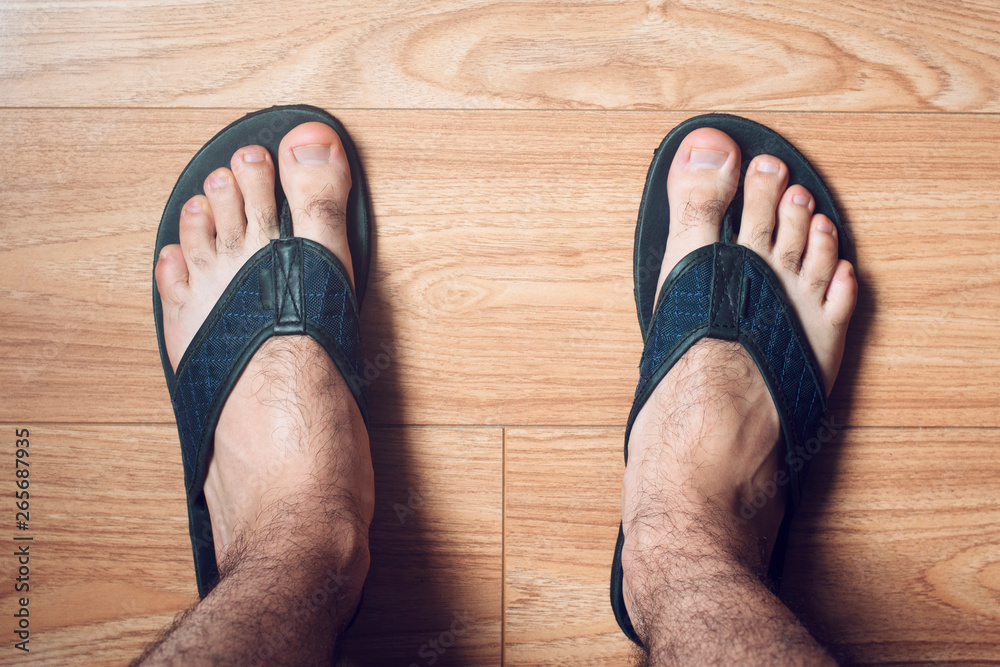 Male hairy feet wearing blue flip flops standing on a brown wooden ...