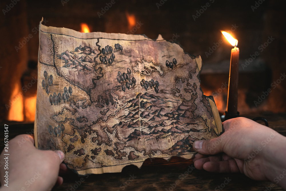 Adventurer man is holding in hands a treasure map over a burning fire ...