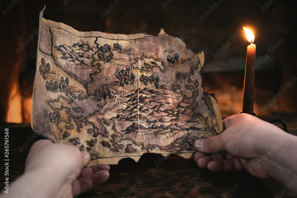 Adventurer man is holding in hands a treasure map over a burning fire ...