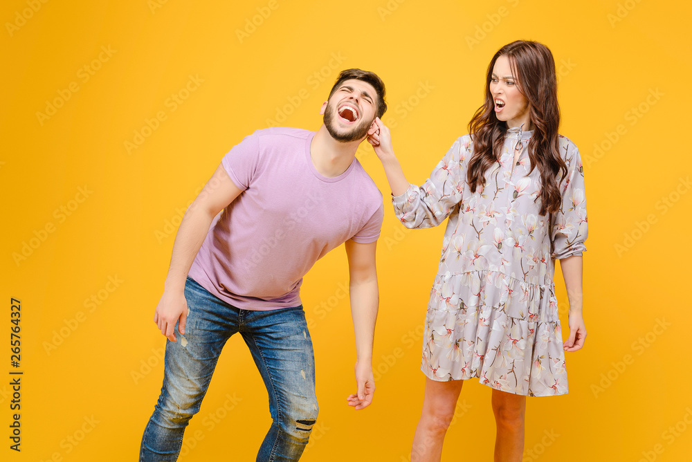 Angry young woman dragging boyfriend holding his ear isolated over ...