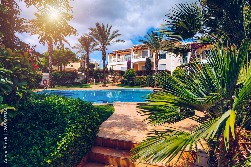 Swimming pool, sun-loungers and palm trees during a warm sunny day ...