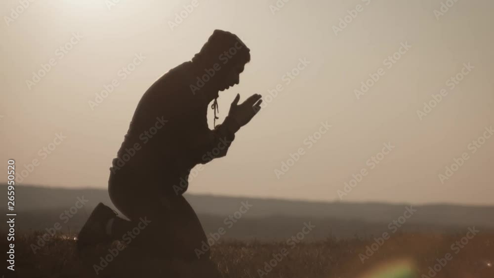 Silhouette young man praying outside at beautiful sunset. Male asks for ...