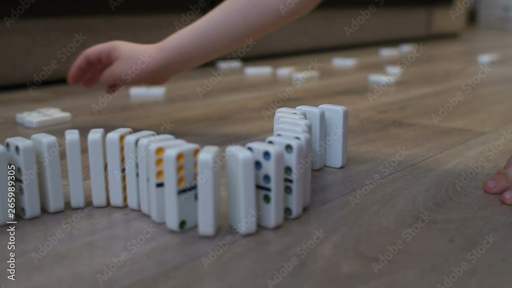 Close-up of a little boy playing dominoes sitting on the wooden floor ...