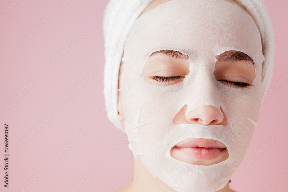 Beautiful young woman is applying a cosmetic tissue mask on a face on a ...