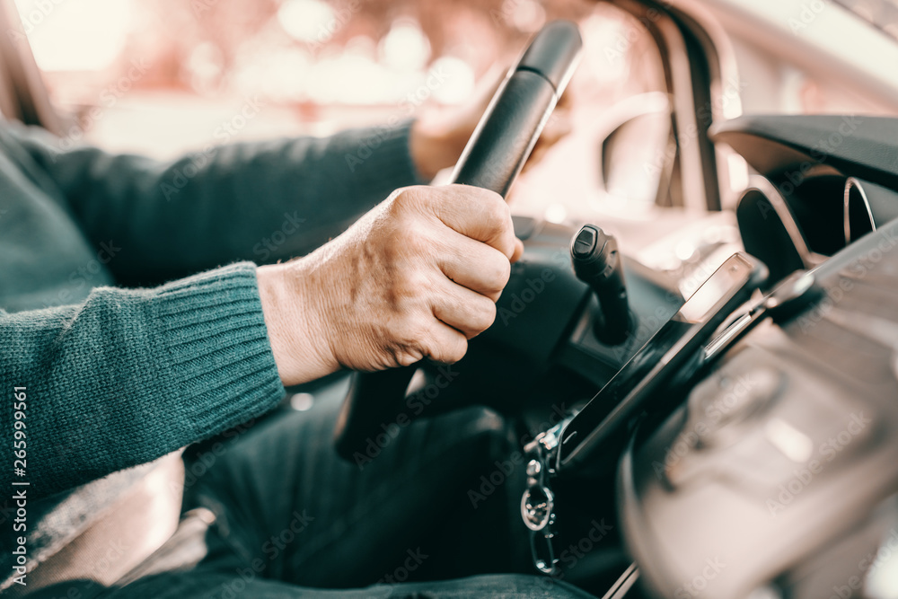 Close up of senior man holding hands on steering while and driving his ...