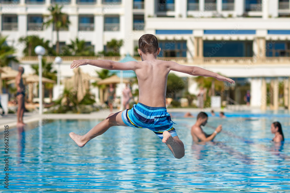 Boy having fun making fantastic jump into swimming pool. His arms are ...