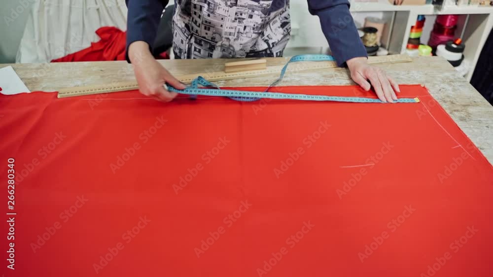 Woman's hands measuring red fabric with blue tape measure on a table ...