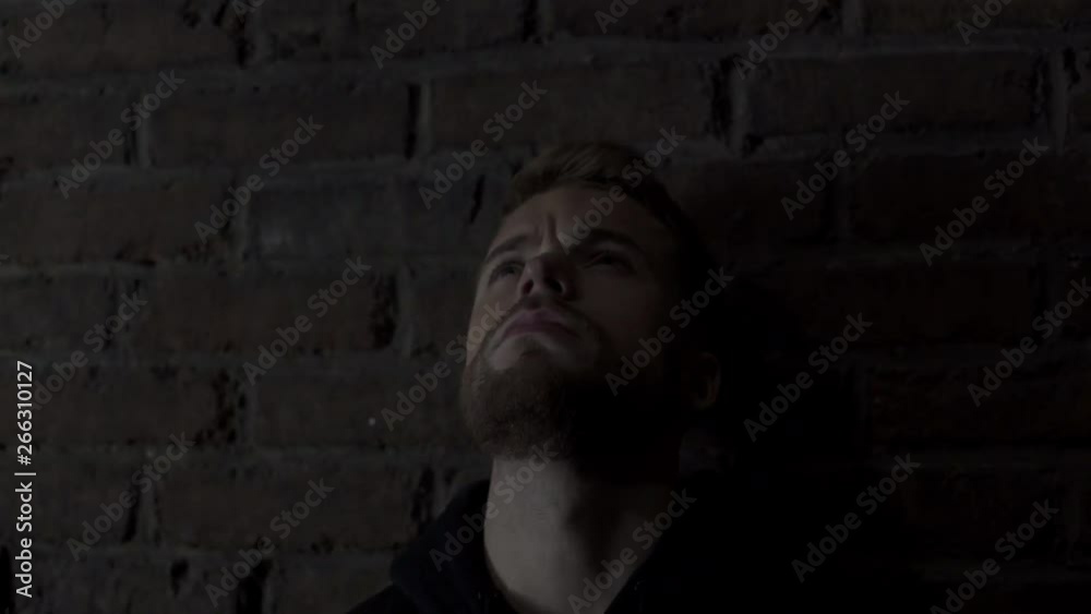 close-up in 4K of a handsome young man leaning against a wall raising ...