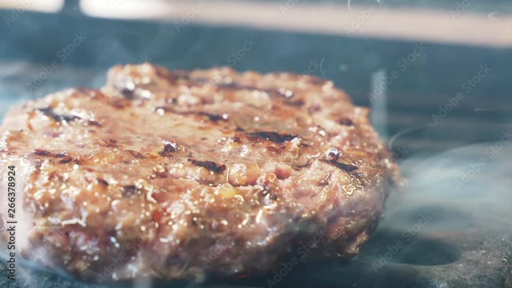 Tasty meat for a burger cooked on a fiery barbecue grill. Close up of ...