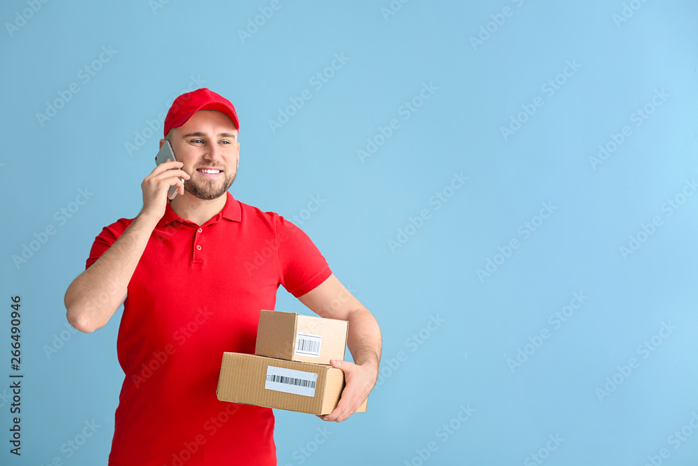 Handsome delivery man with boxes talking by phone on color background ...